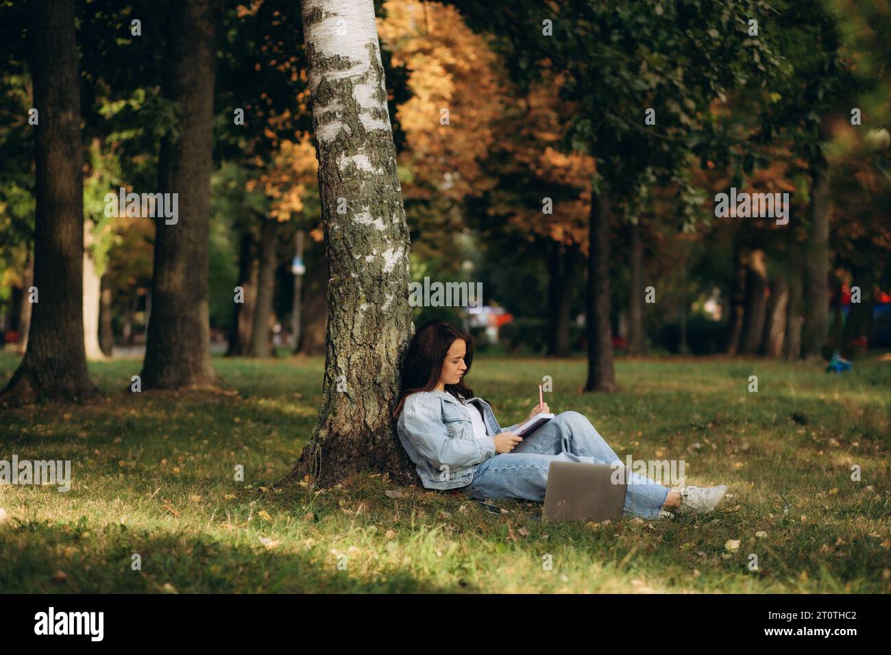 woman under tree with laptop and notepad Stock Photo - Alamy