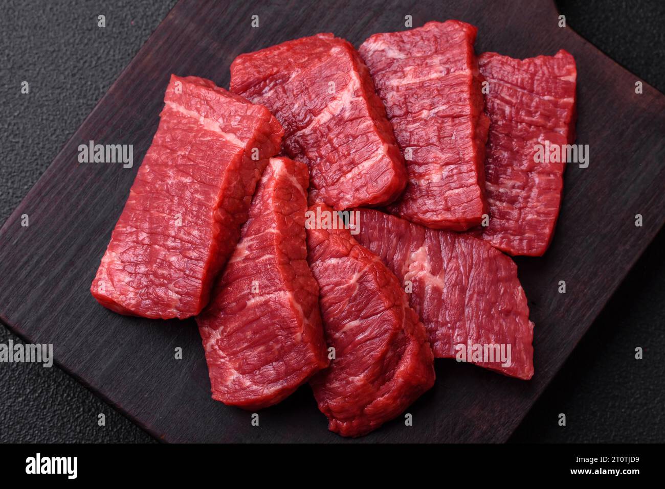 Fresh juicy raw beef slices with salt and spices on a dark concrete ...
