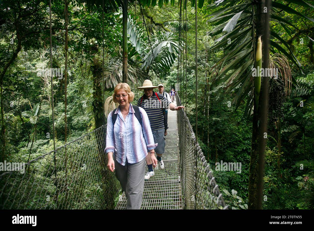 Hikers at the Arenal rainforest reserve walking on a hanging bridge. La ...