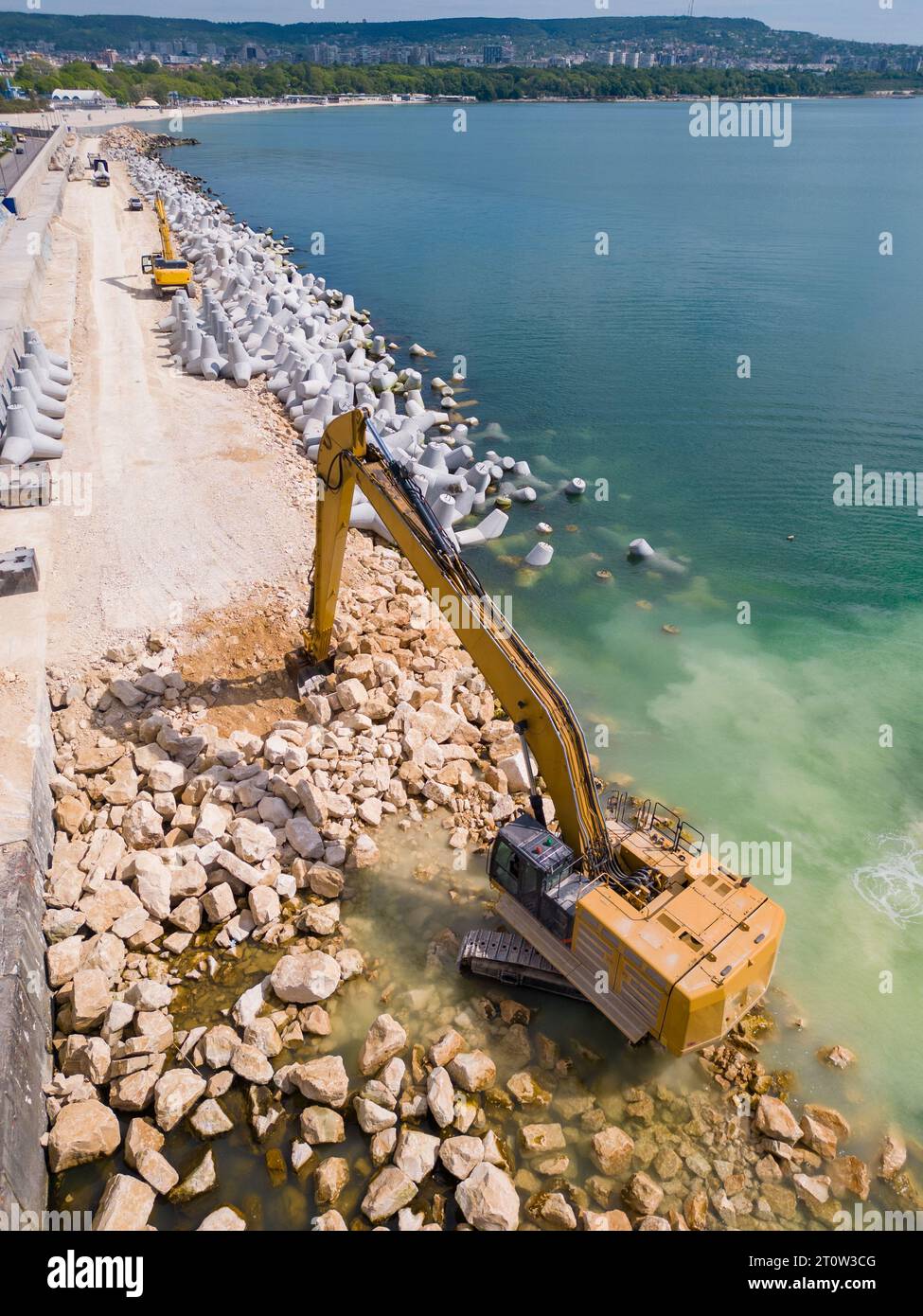 An excavator diligently constructs a dock or breakwater in the sea, its ...