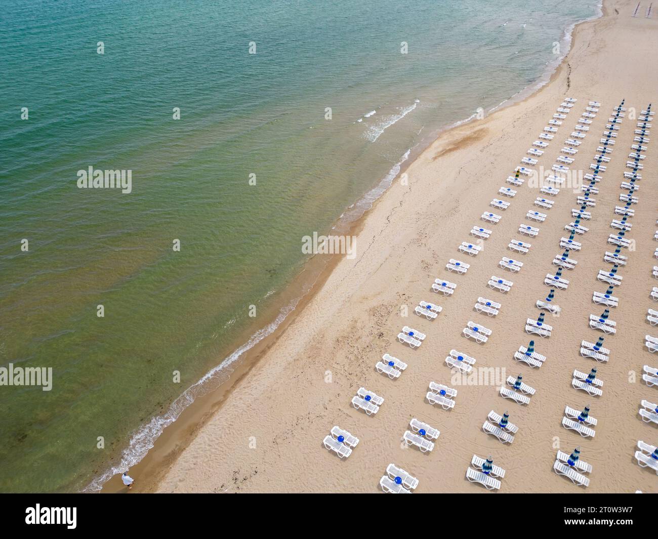 A sandy beach stretches along the seaside, adorned with empty sun ...