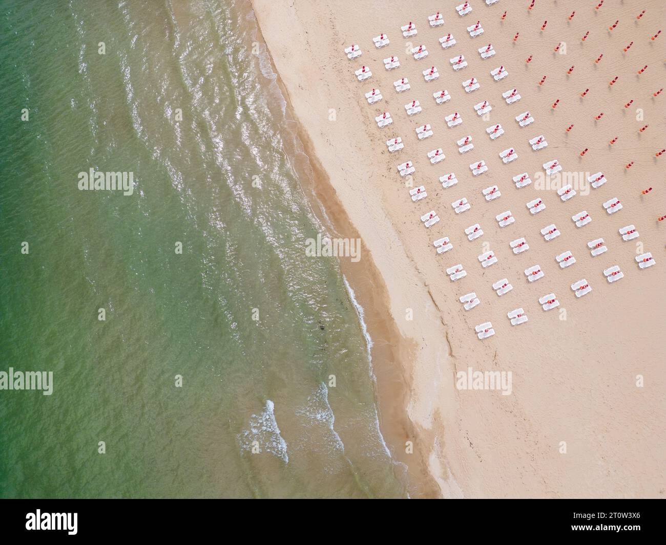 A sandy beach stretches along the seaside, adorned with empty sun ...