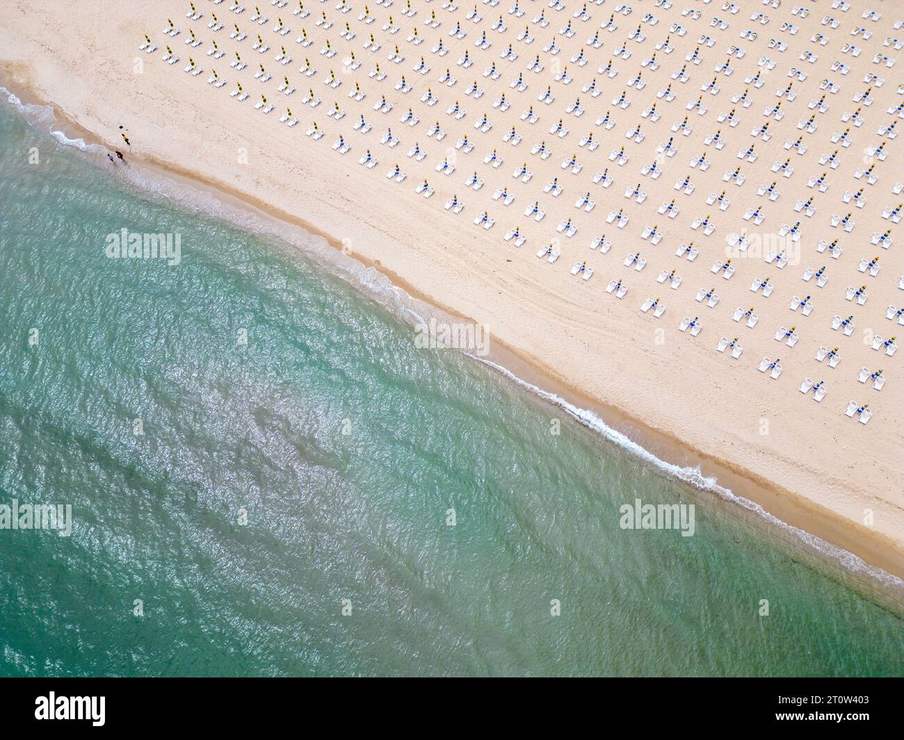 A sandy beach stretches along the seaside, adorned with empty sun ...