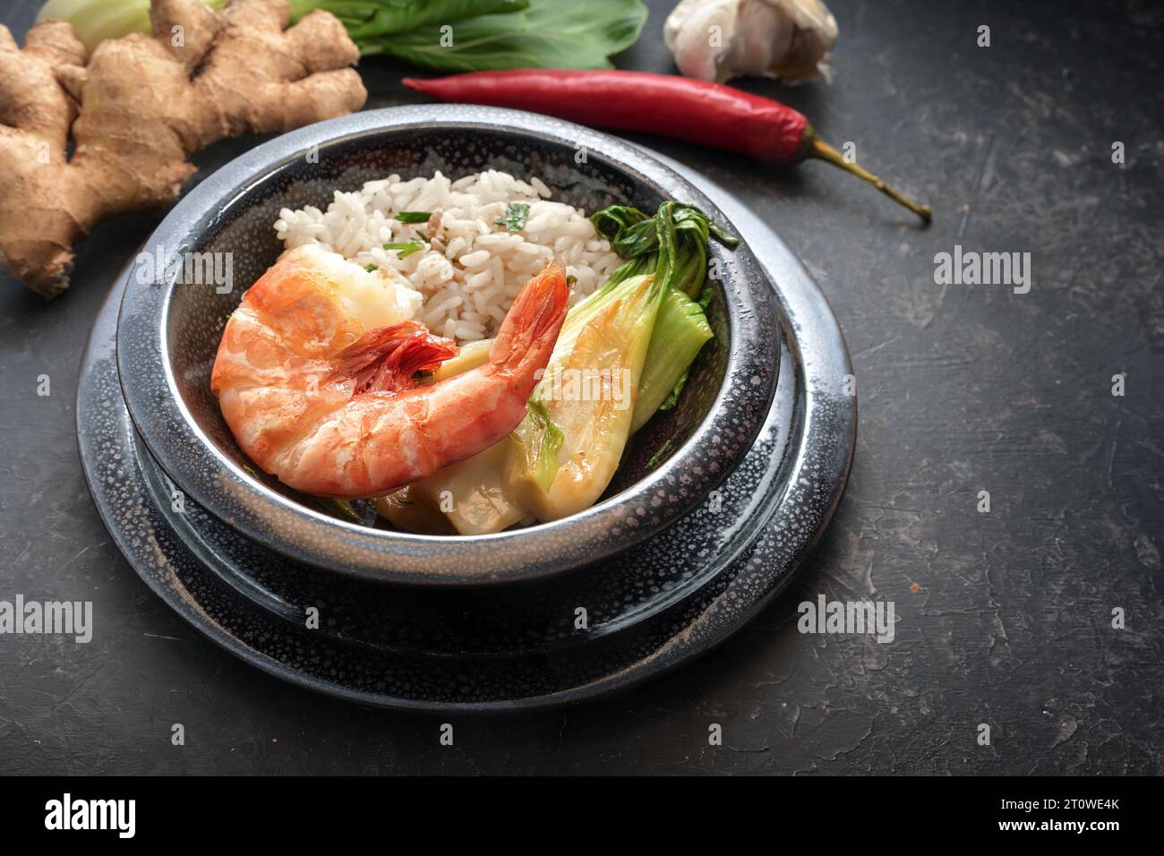 Tiger prawn or shrimp with pak choi and rice in a black ceramic bowl on ...