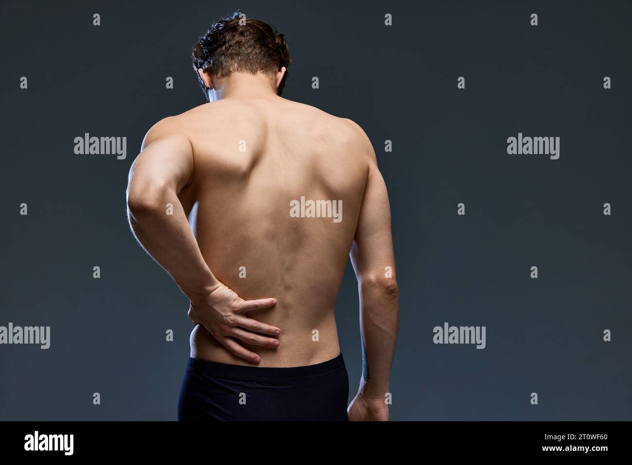 Rear view portrait of young brunette man posing, holding his muscular ...