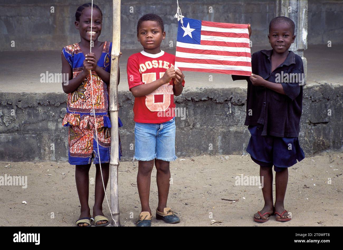 Liberia, Monrovia; children raise the liberian flag in front of their ...