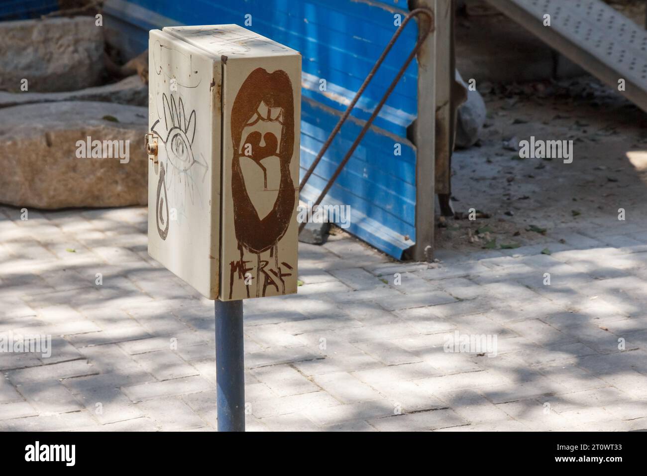 A metal box on top of a metallic pole by a city street. The object has ...