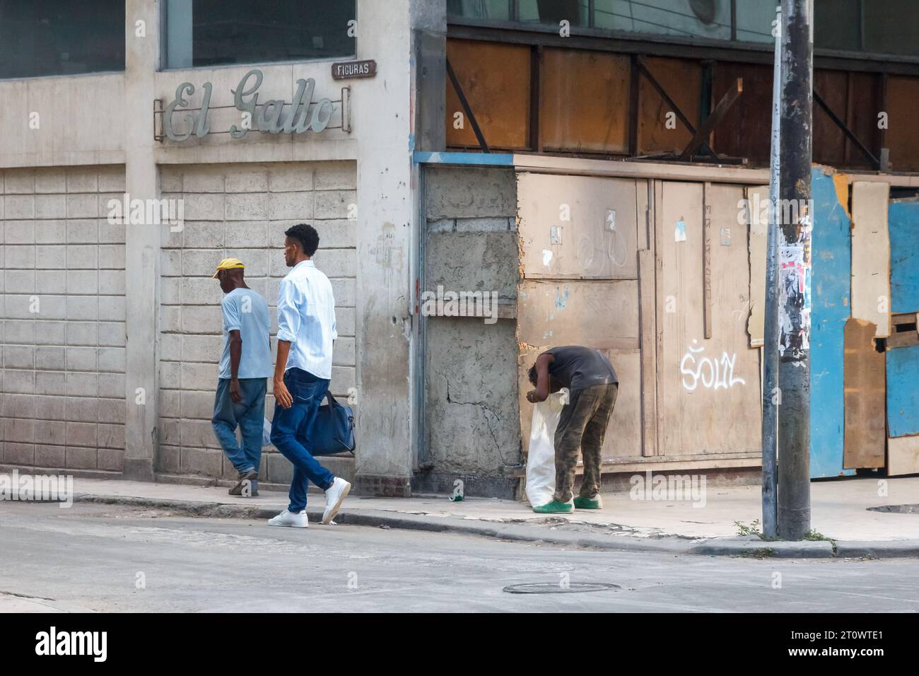 An Afro-Caribbean Cuban man looks inside a sack below a porch of a run ...