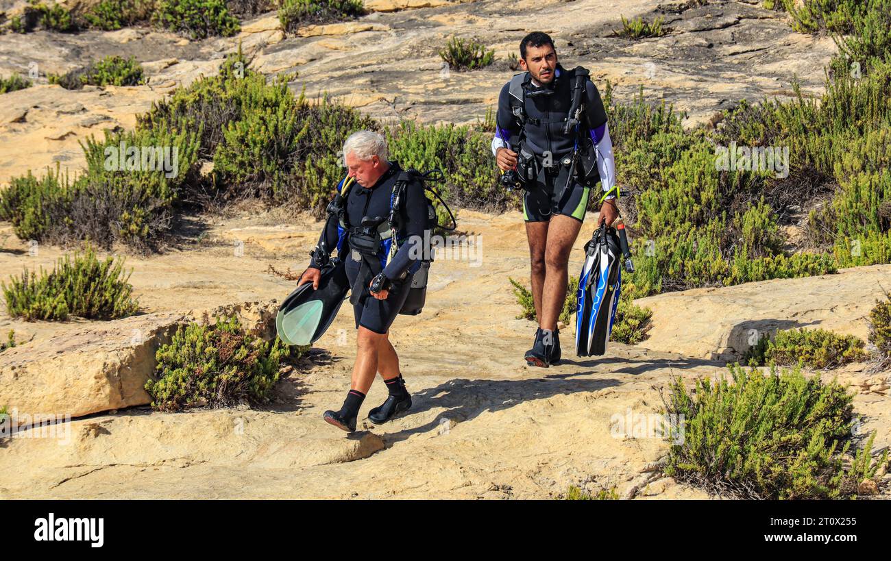 TWO DIVERS HEAD TOWARDS THE SEA AT XATT L-AHMAR ON THE MEDITERRANEAN ...