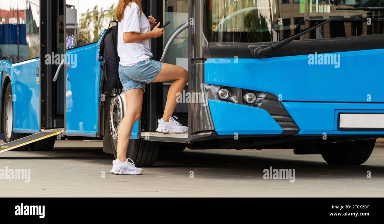 Urban woman passenger gets on the bus at a bus stop in city in summer ...