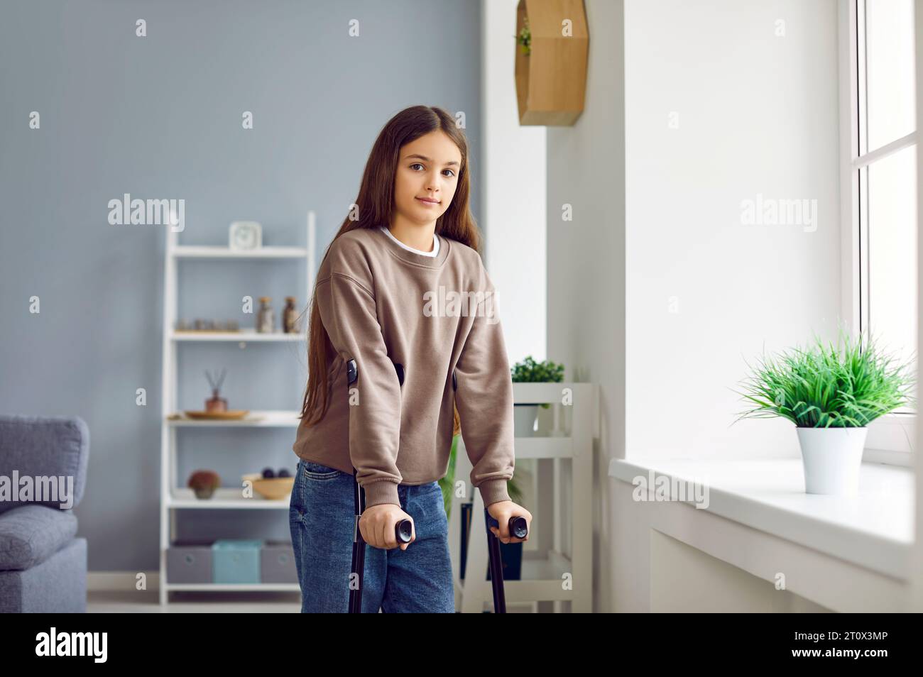 Portrait of child girl with leg injury standing with crutches in living ...