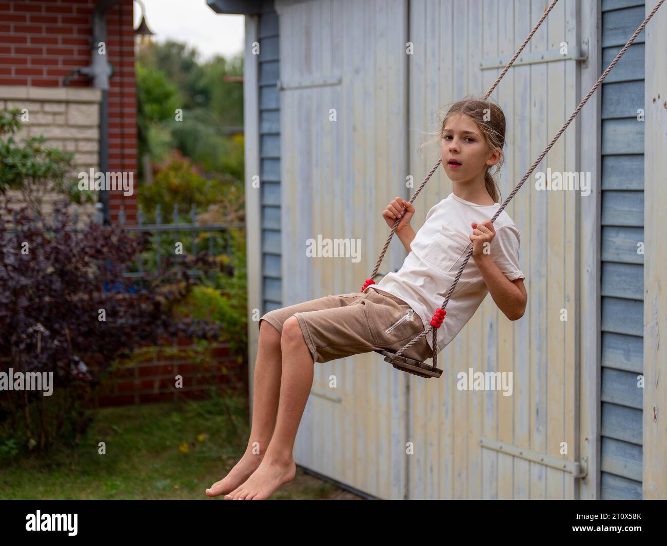 Boy swinging while sitting on children's swing at shed and garden gate ...