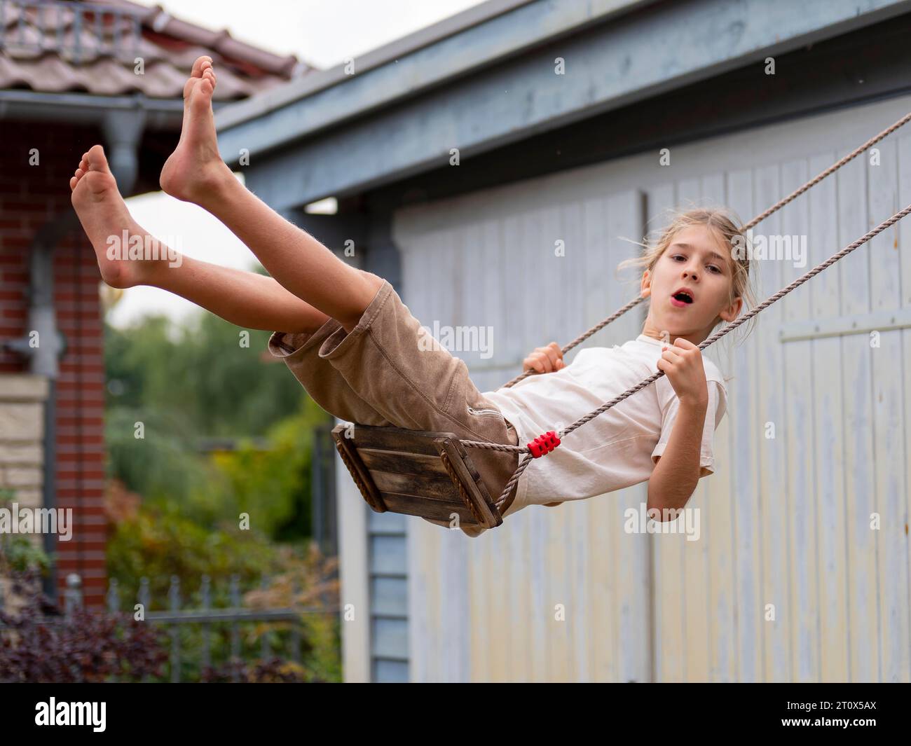 Boy swinging while sitting on children's swing at shed and garden gate ...