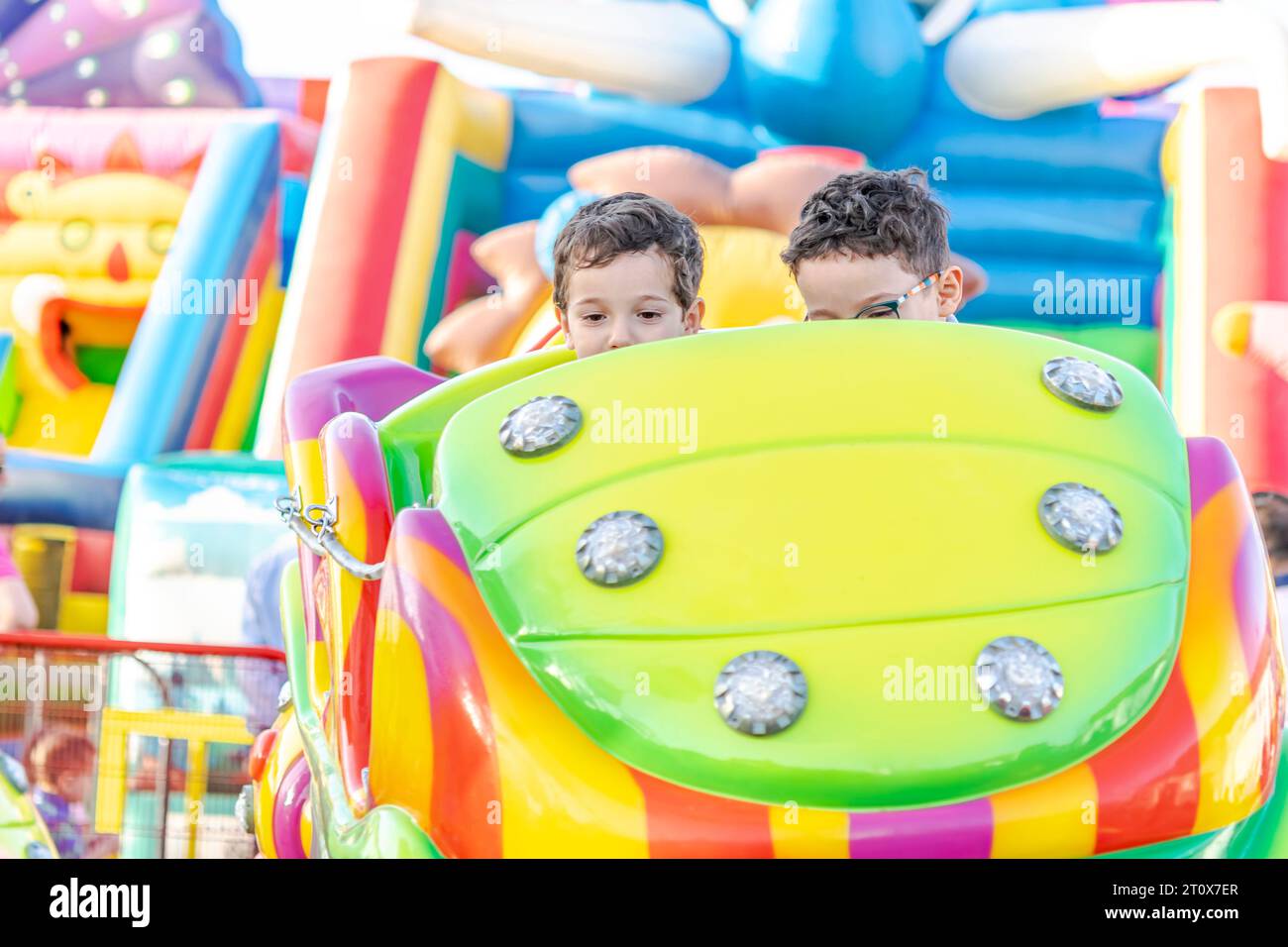 Two little boys sitting in a bright yellow, green, orange and red ...