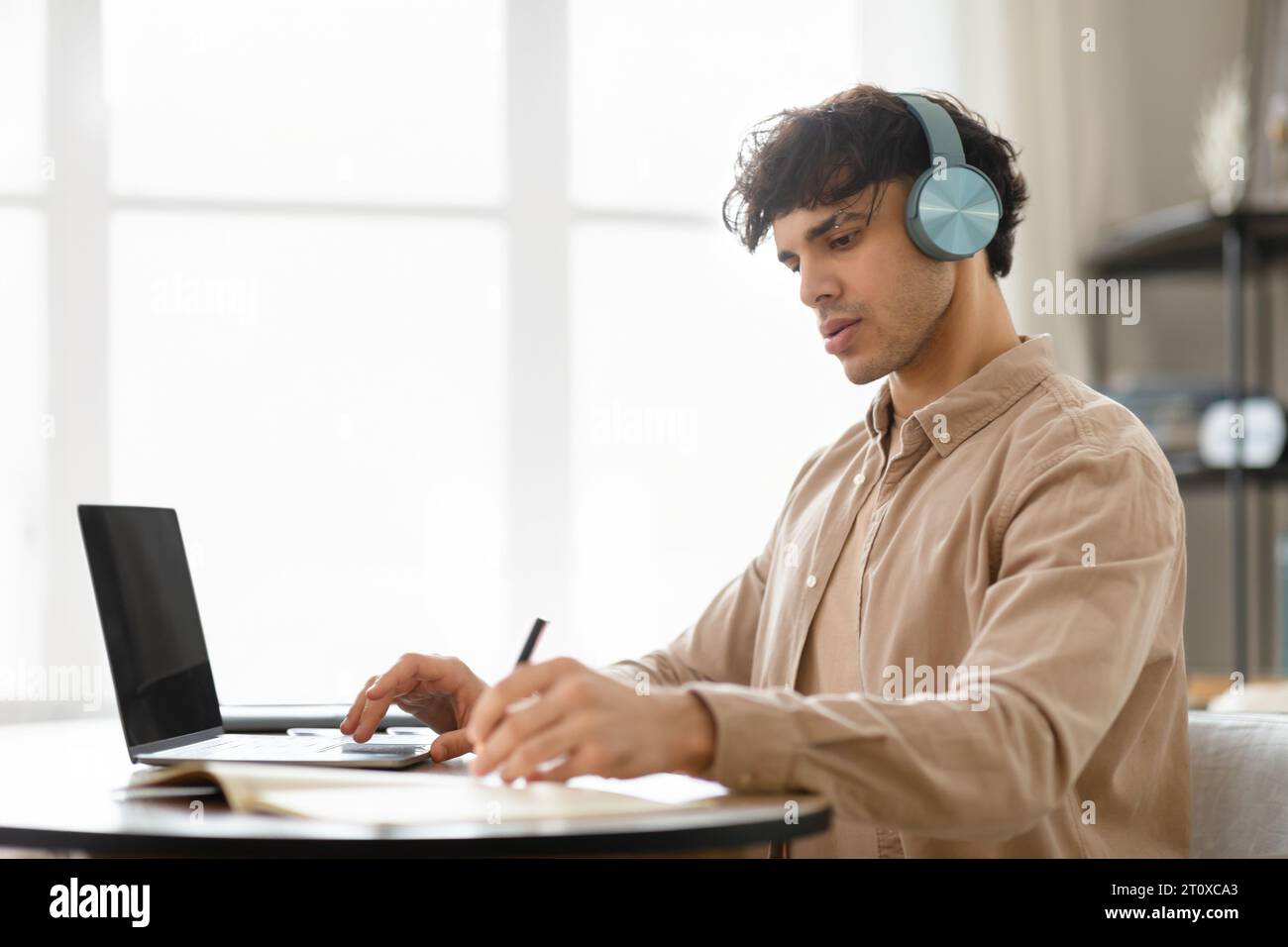 Arab Man At Laptop Writing Notes Wearing Wireless Earphones Indoors ...