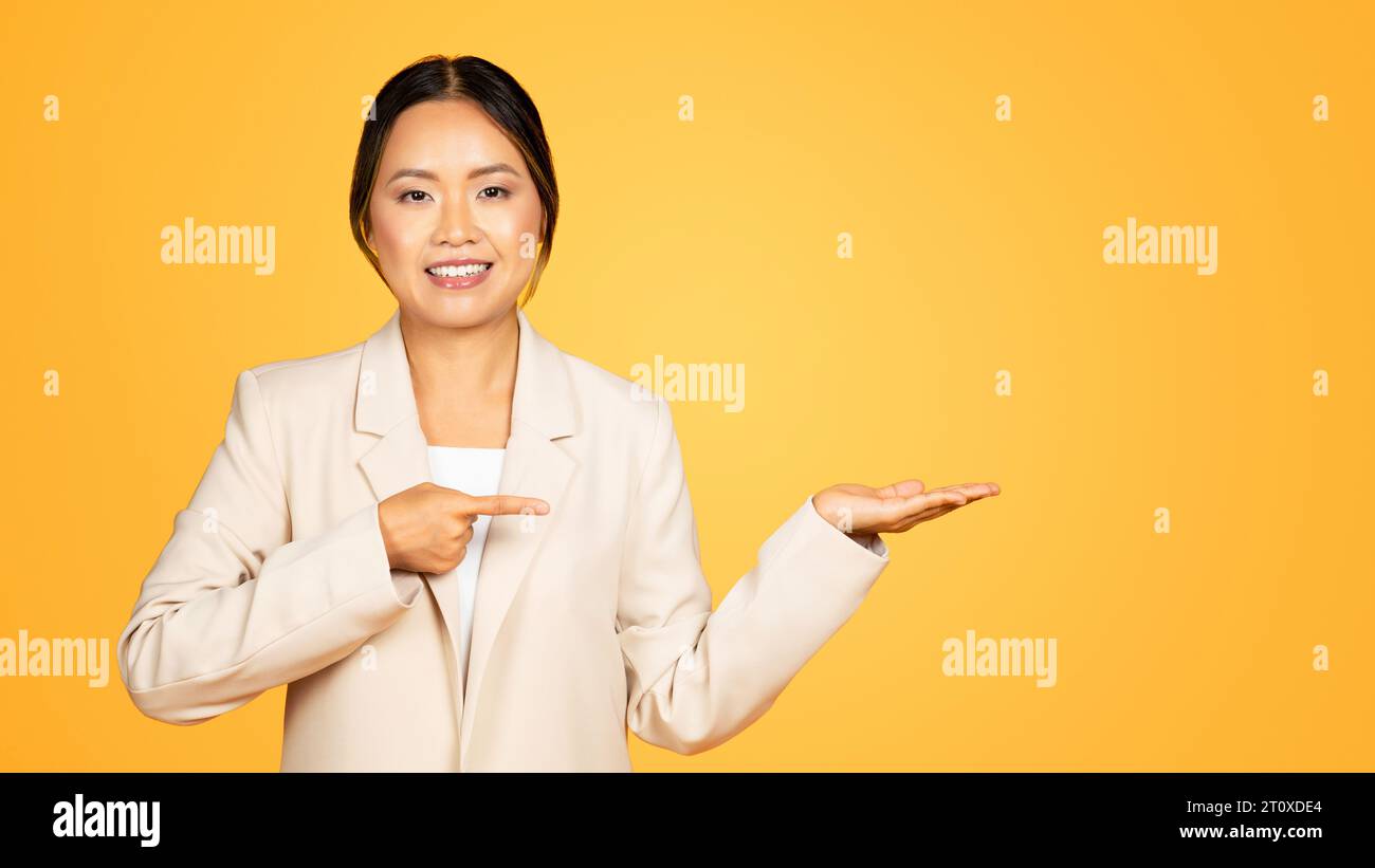 Smiling Asian woman pointing finger, engaging with ample free space ...