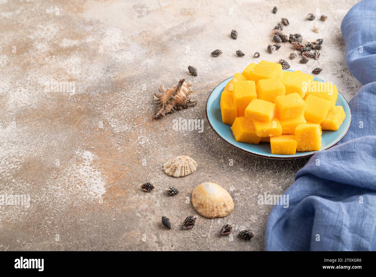 Dried and candied mango cubes on blue plate on brown concrete ...