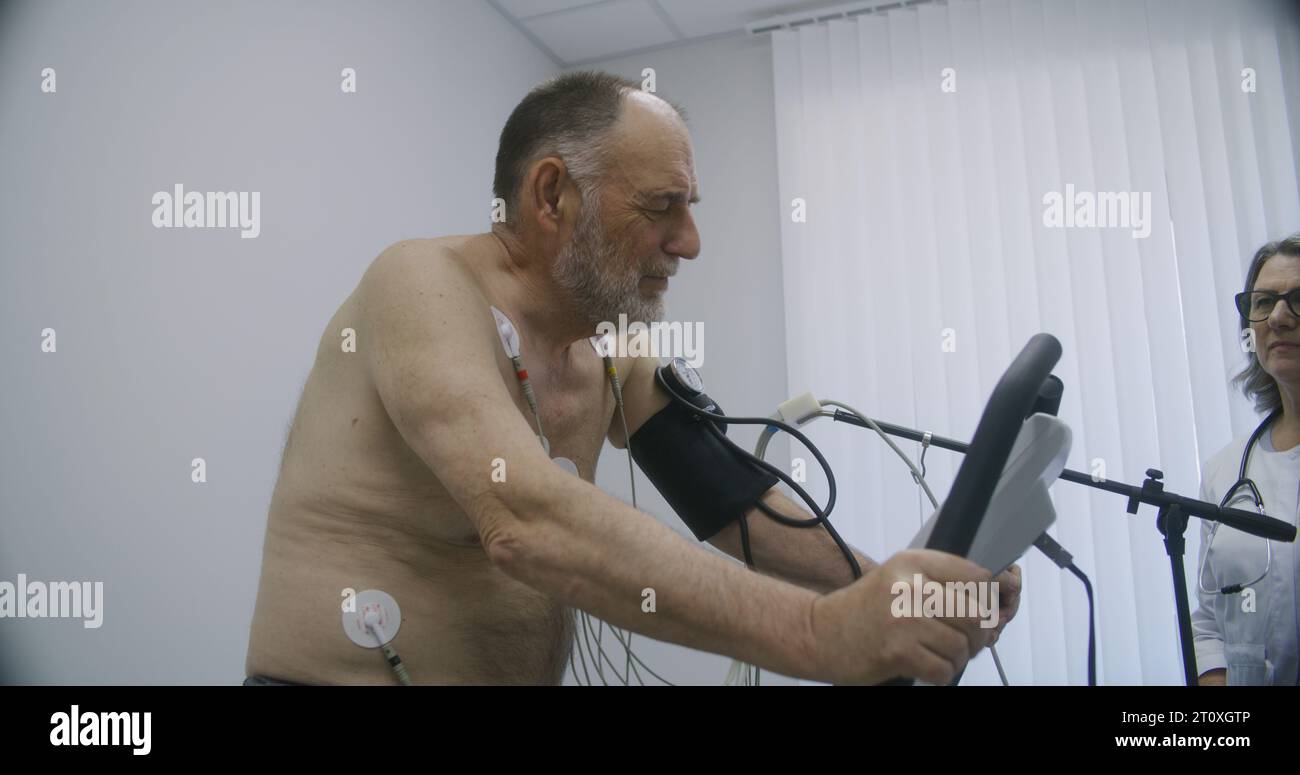 Elderly man with holter sensors pedals orbitrek in cardiology room ... Elderly man with holter sensors pedals orbitrek in cardiology room ...