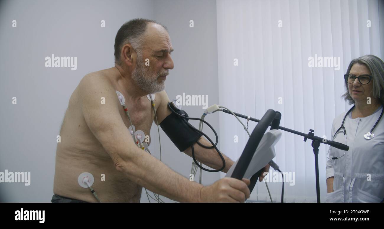 Elderly man with holter sensors pedals orbitrek in cardiology room ...