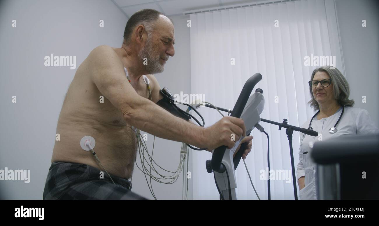 Elderly man with holter sensors pedals orbitrek in cardiology room ...