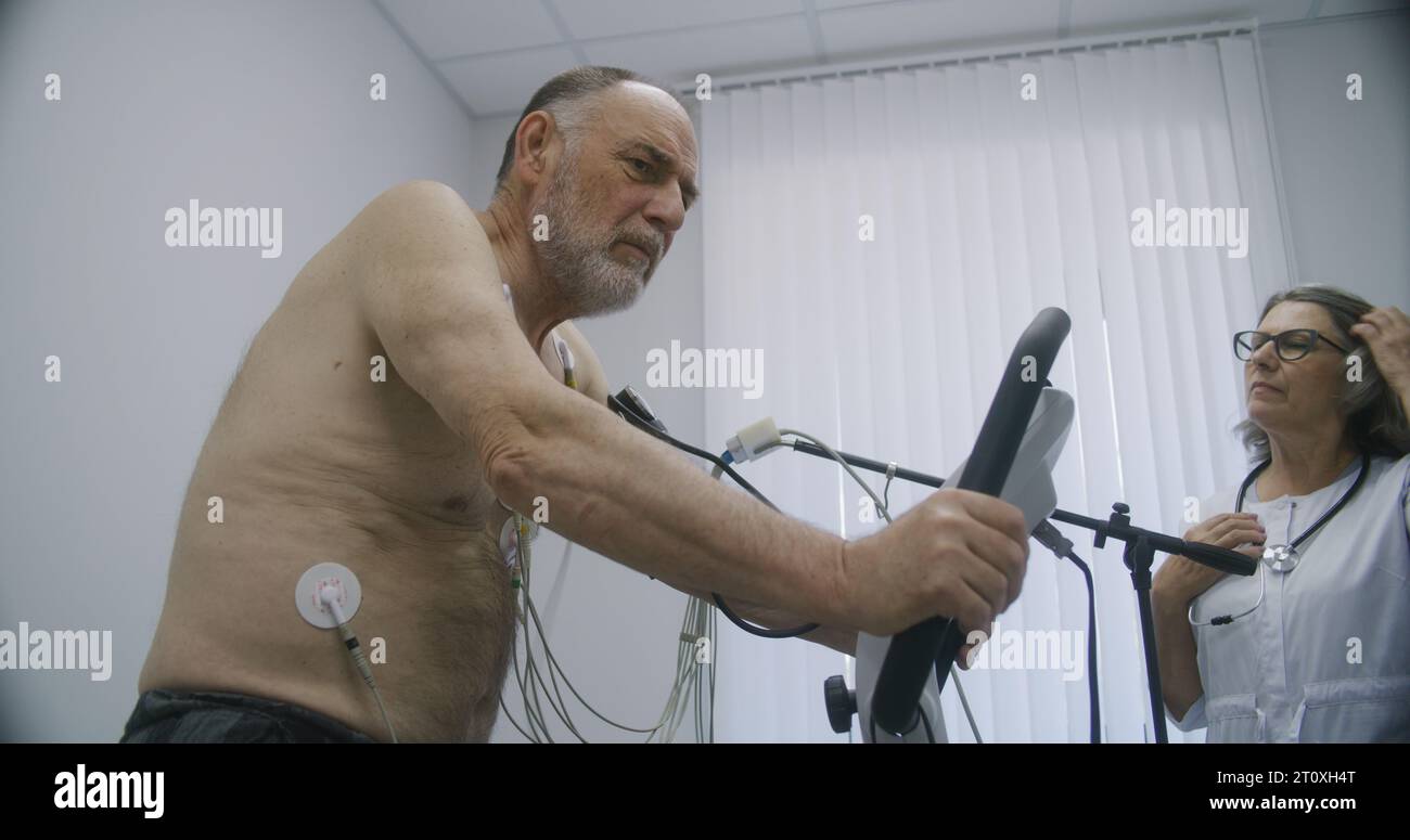 Elderly man with holter sensors pedals orbitrek in cardiology room ...
