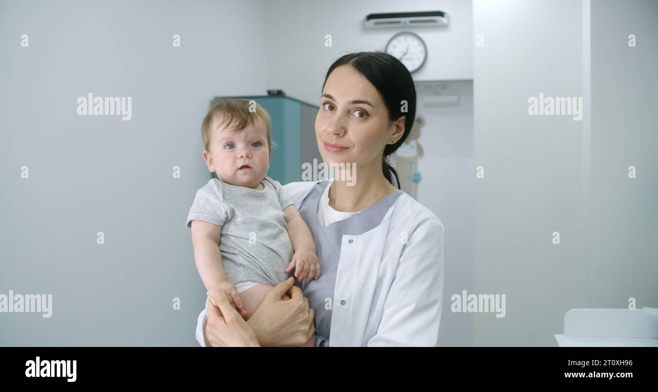 Female pediatrician stands in middle of bright hospital room and looks ...