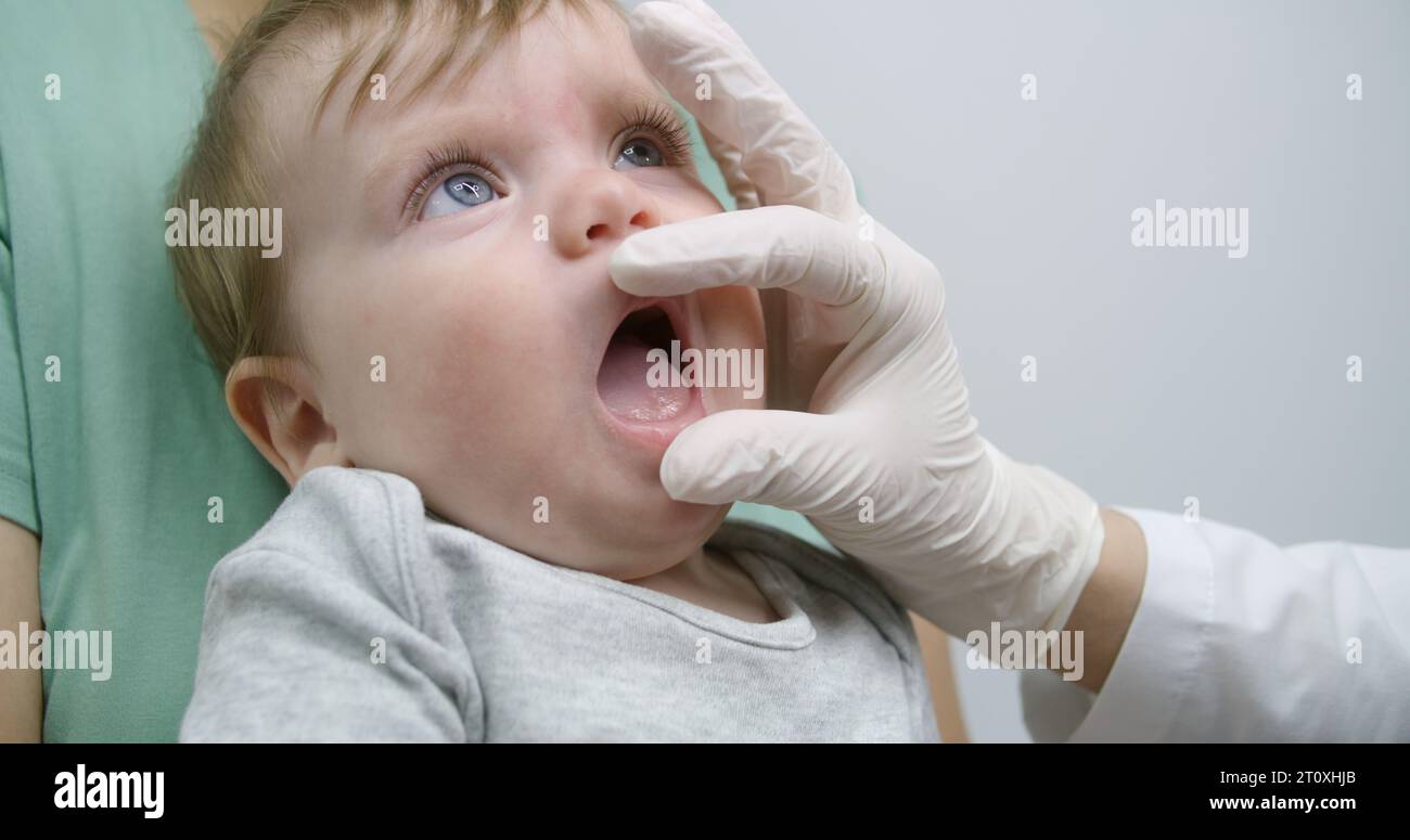 Baby sits in arms of mother and cries. Female doctor tries to check ...