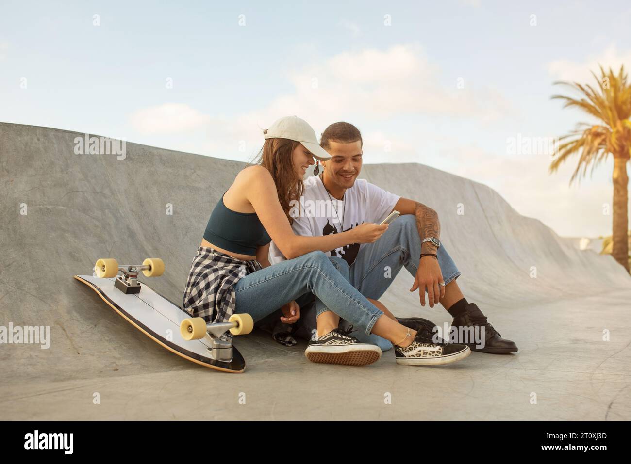 Skateboarding couple pauses to use cellphone outdoors Stock Photo - Alamy