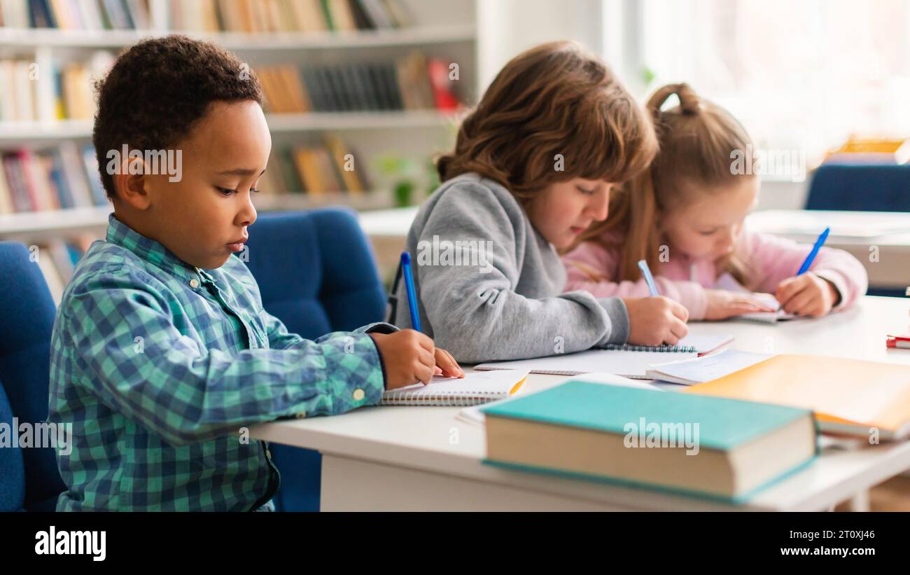 Diverse primary school children writing in copybooks during a test ...