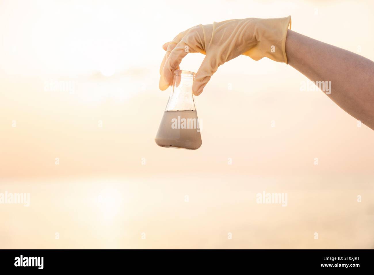 Close-up of hand wearing rubber glove holding flask with sample of ...