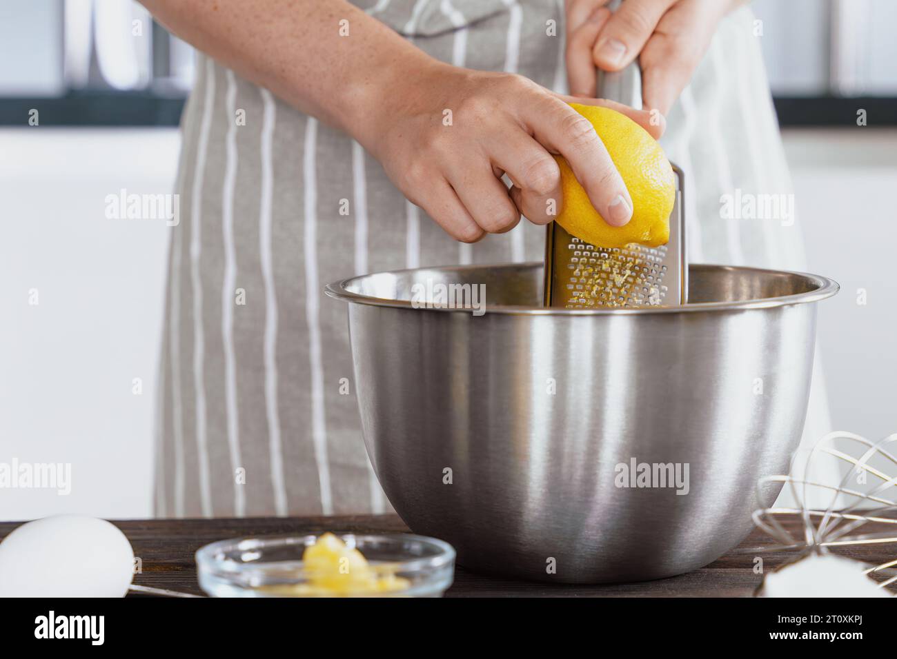 The cook's hands grate the zest of a lemon into a bowl of dough ...