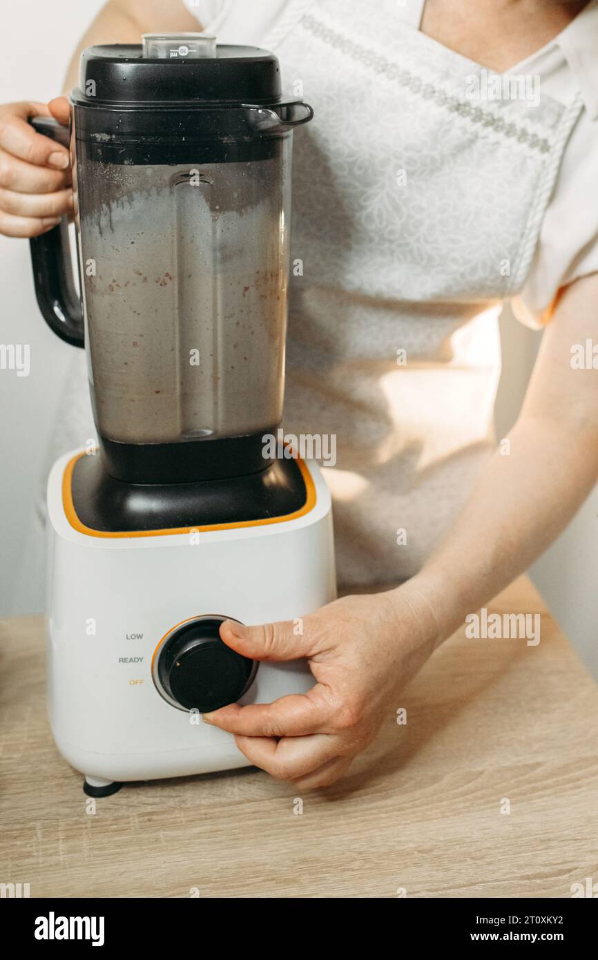 A woman turns on the mixer and prepares a milkshake. Vertical frame ...