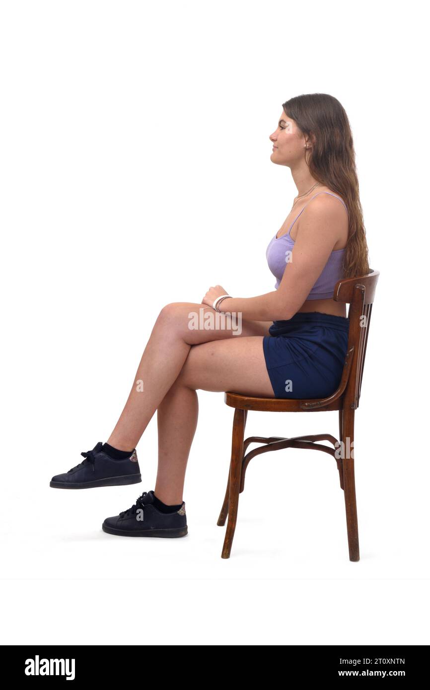 side view of a young girl sitting on chair cross legged on white ...