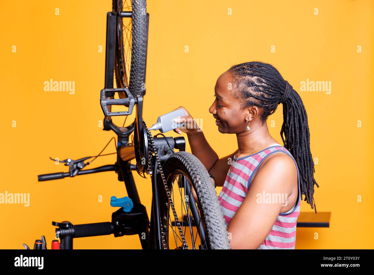 African American female cyclist carefully examines and repairs bike ...