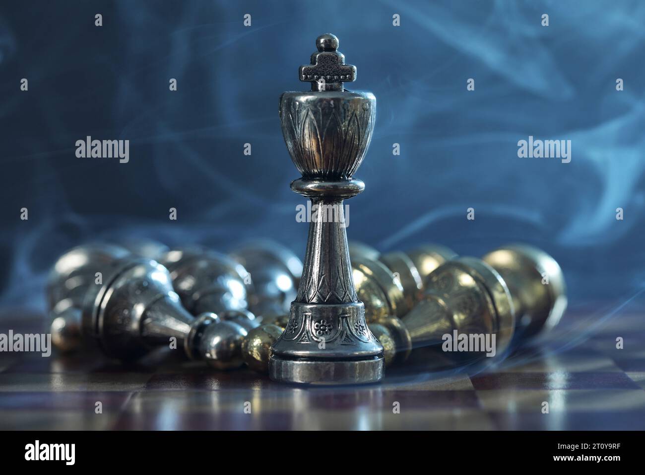King among fallen chess pieces on checkerboard against dark background ...