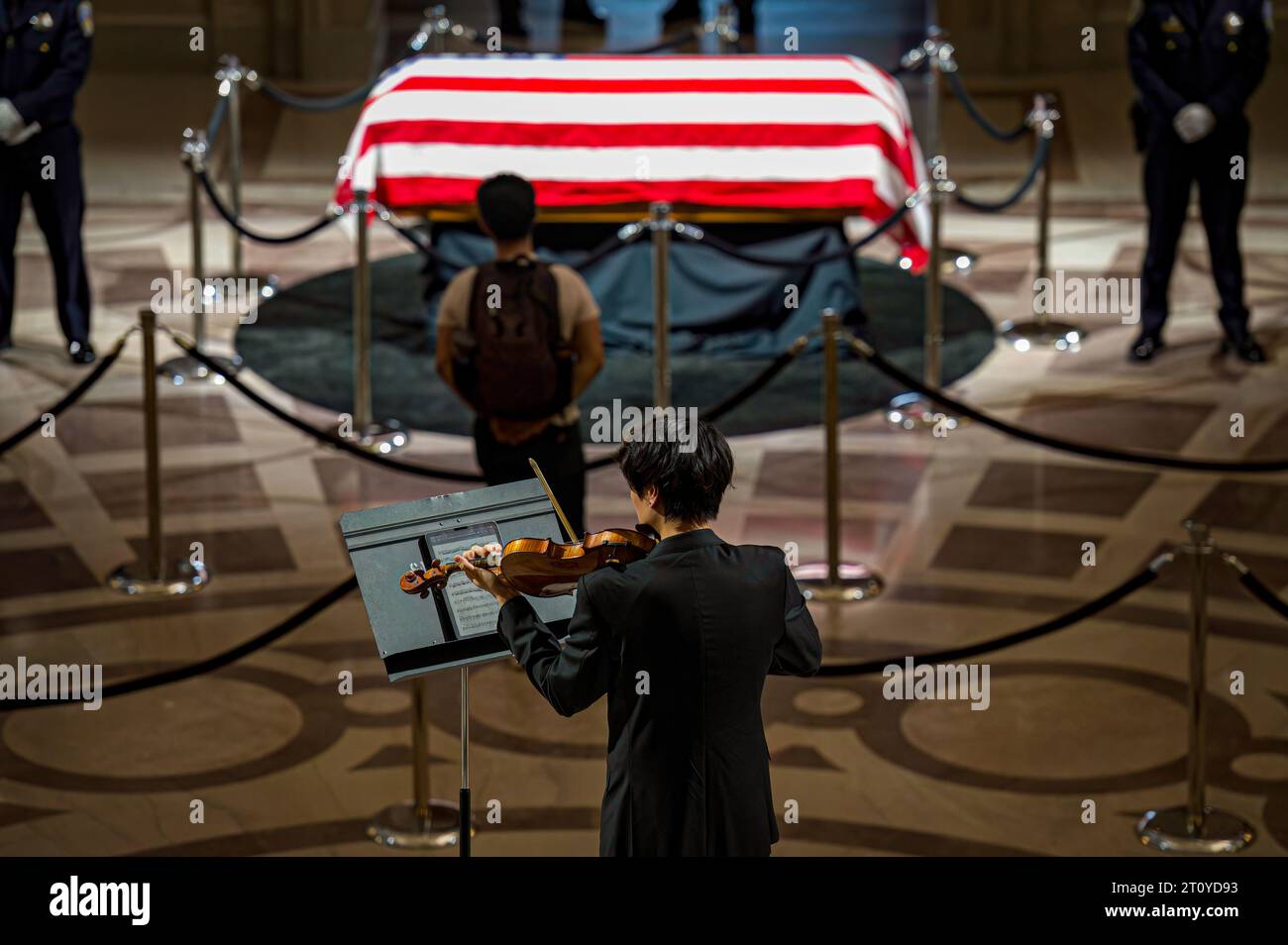 A solo violinist players while a person pauses in front of Senator ...