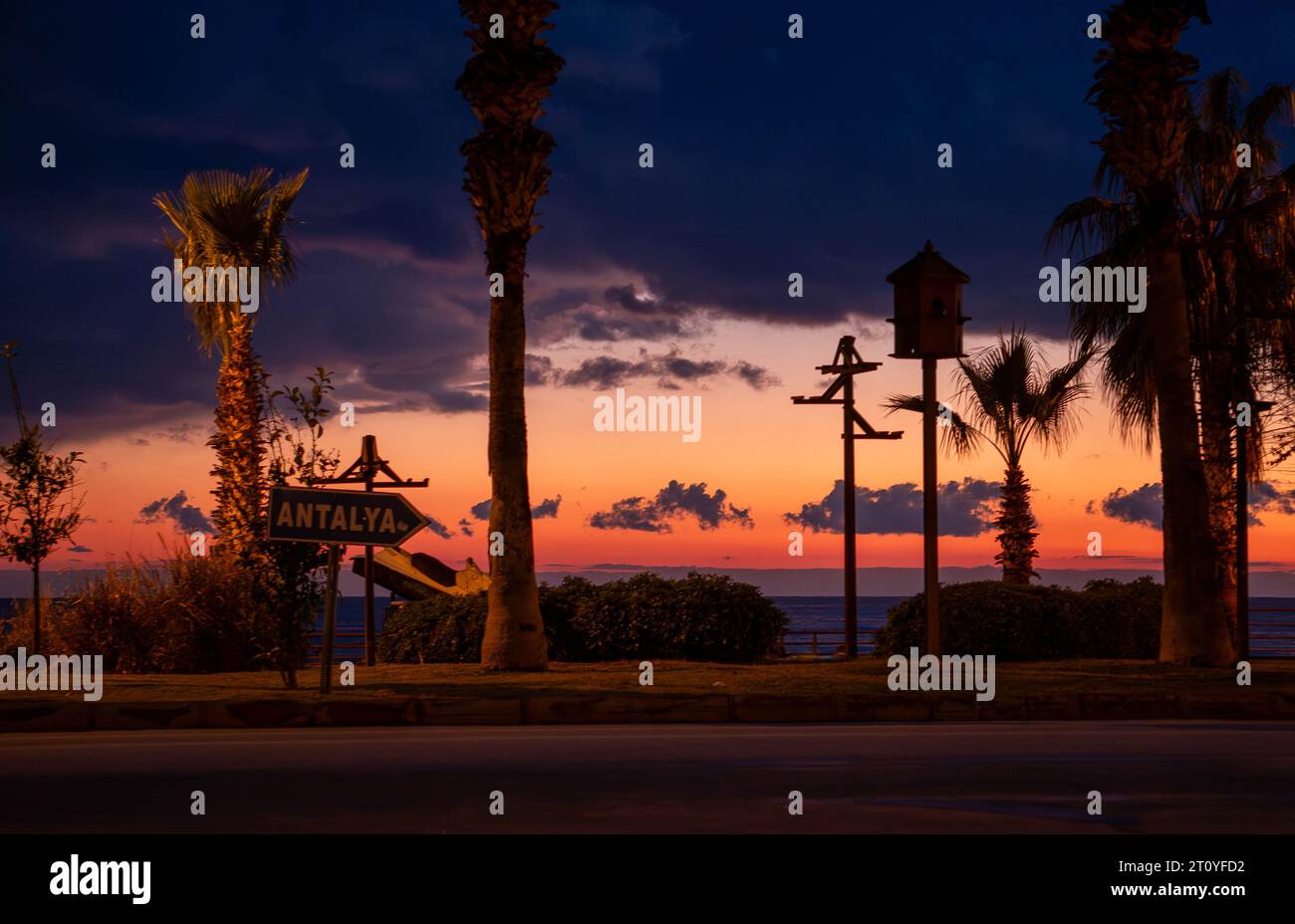 Promenade along the sea with palm trees at sunset. Sign with ...
