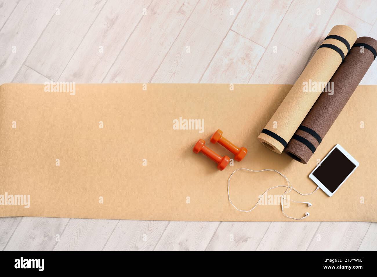 Tablet computer with earphones and dumbbells on fitness mat in room ...