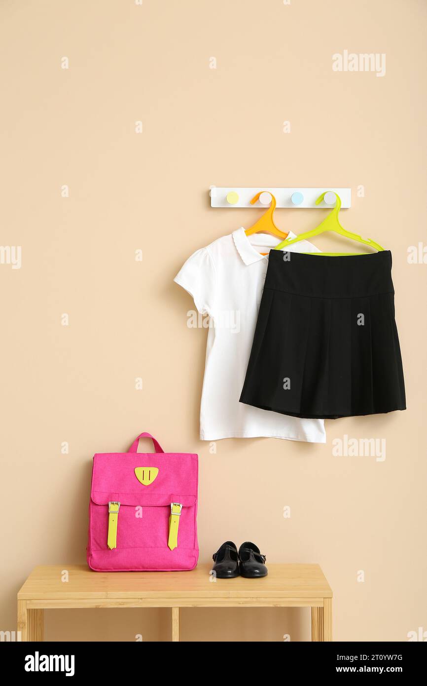 Stylish school uniform hanging on rack with backpack against beige wall ...
