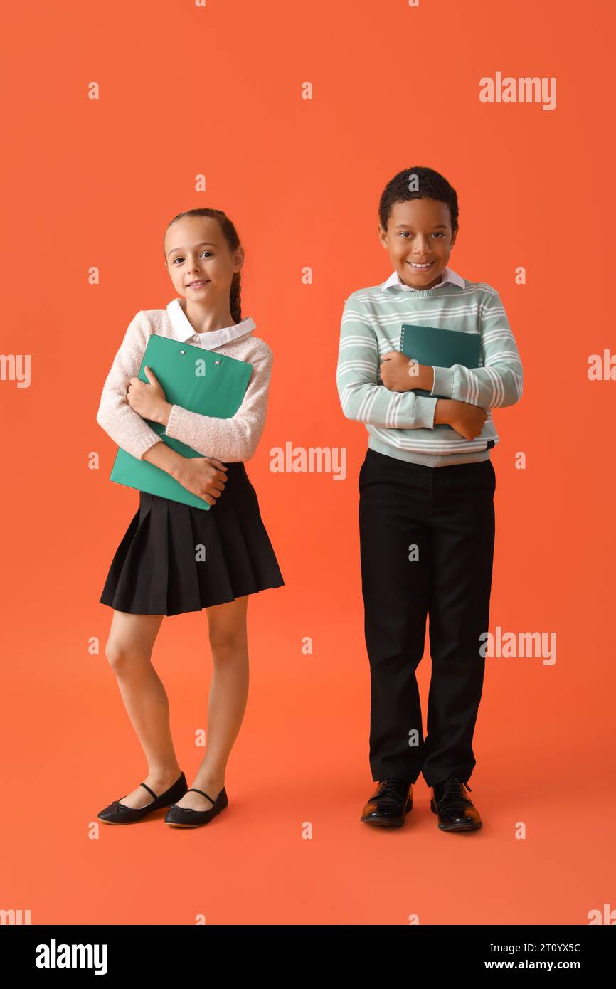 Little classmates in stylish uniform with notebooks on orange ...