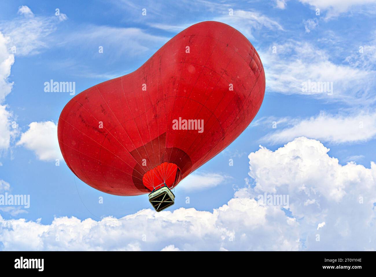 Red heart-shaped hot air balloon flying under a blue sky with white ...