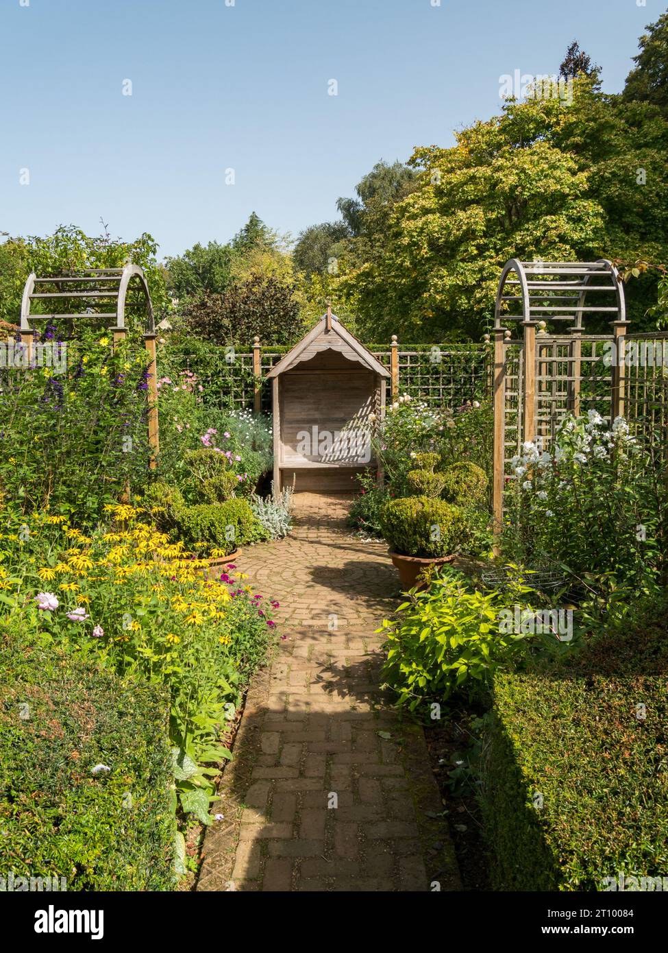 Pretty cottage garden with arbor seat, brick path and trellis in late ...
