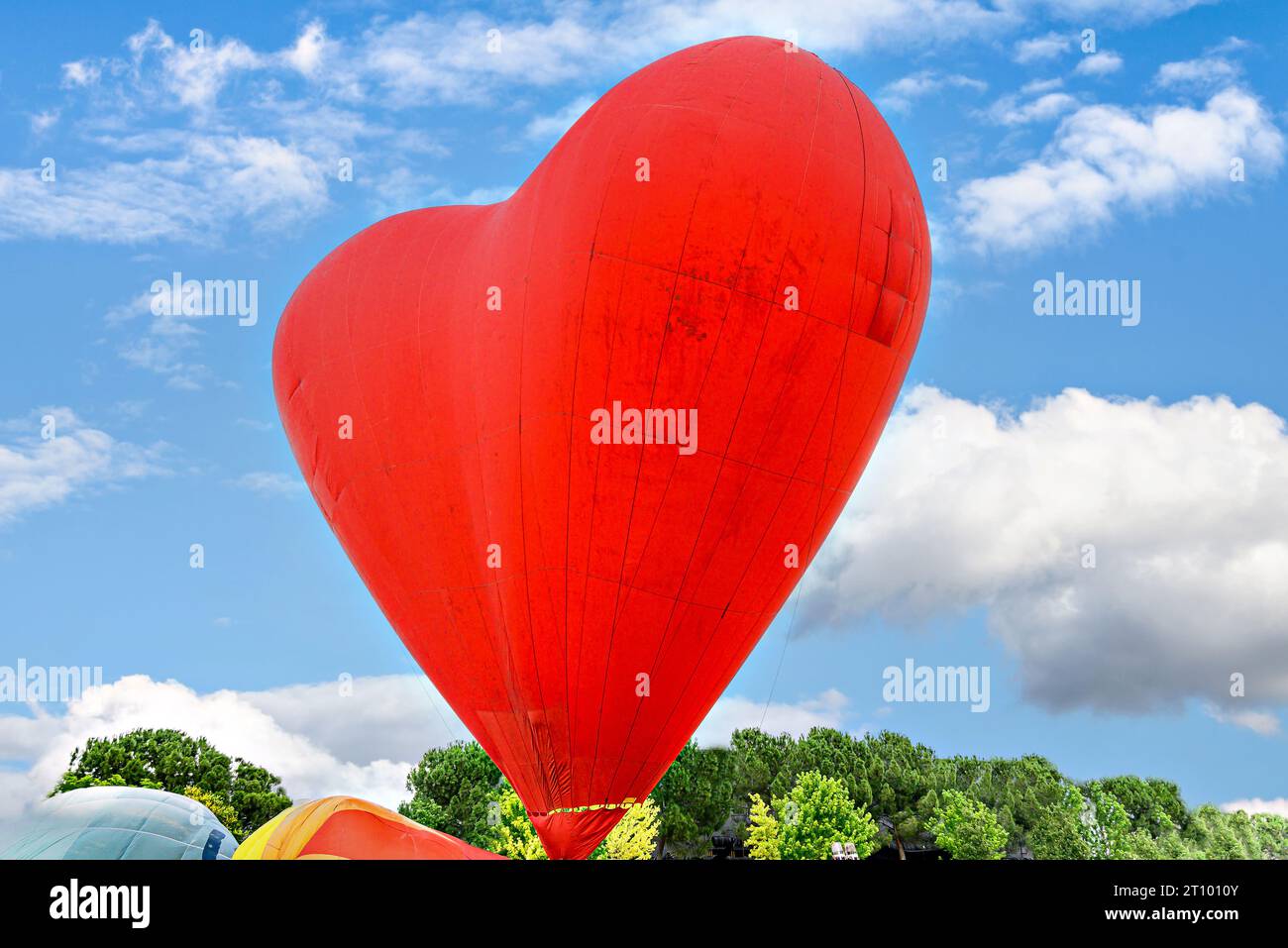 Red heart-shaped hot air balloon flying under a blue sky with white ...