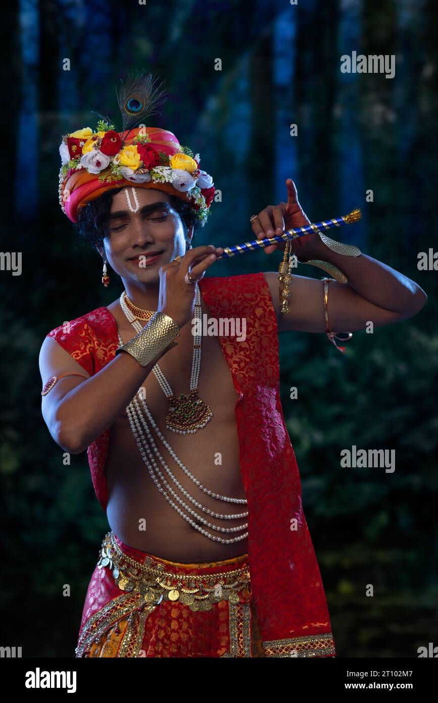 Portrait of young man dressed up as Lord Krishna and playing flute on ...