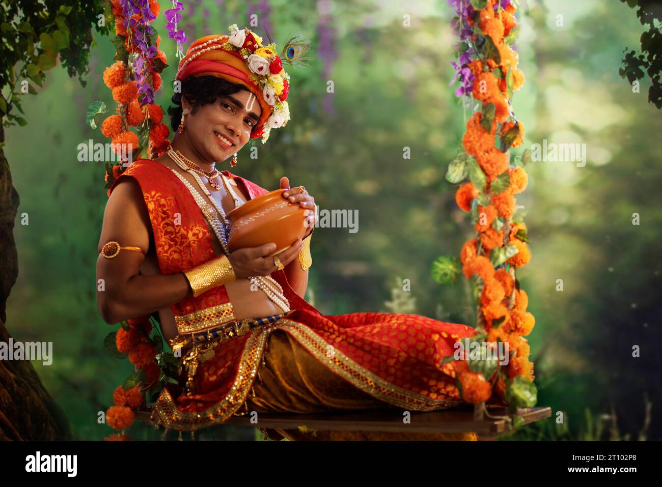 Young man dressed up as Lord Krishna and sitting on a swing with a ...