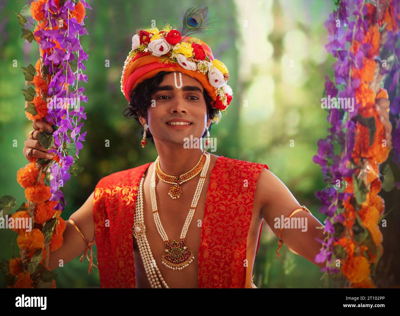 Young man dressed up as Lord Krishna and sitting on a swing on the ...