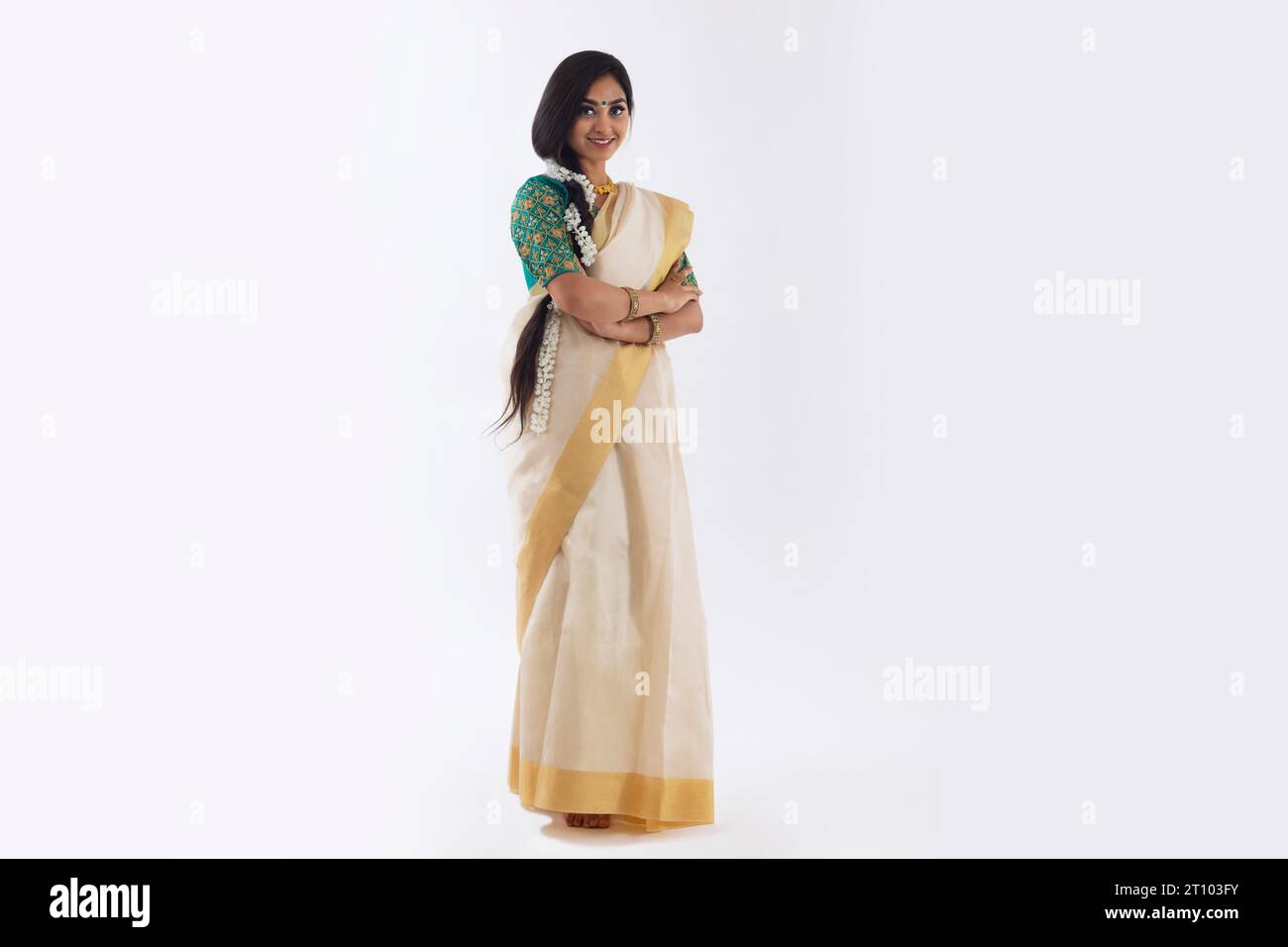 South Indian woman in traditional clothing standing with folded arms against white background ...
