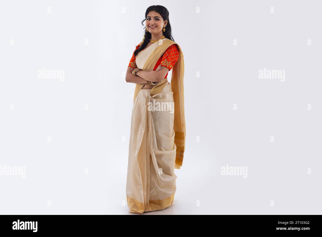 South Indian woman in traditional clothing standing with folded arms against white background ...