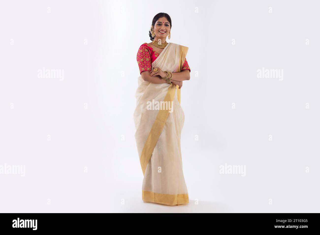 South Indian woman in traditional clothing standing with folded arms against white background ...