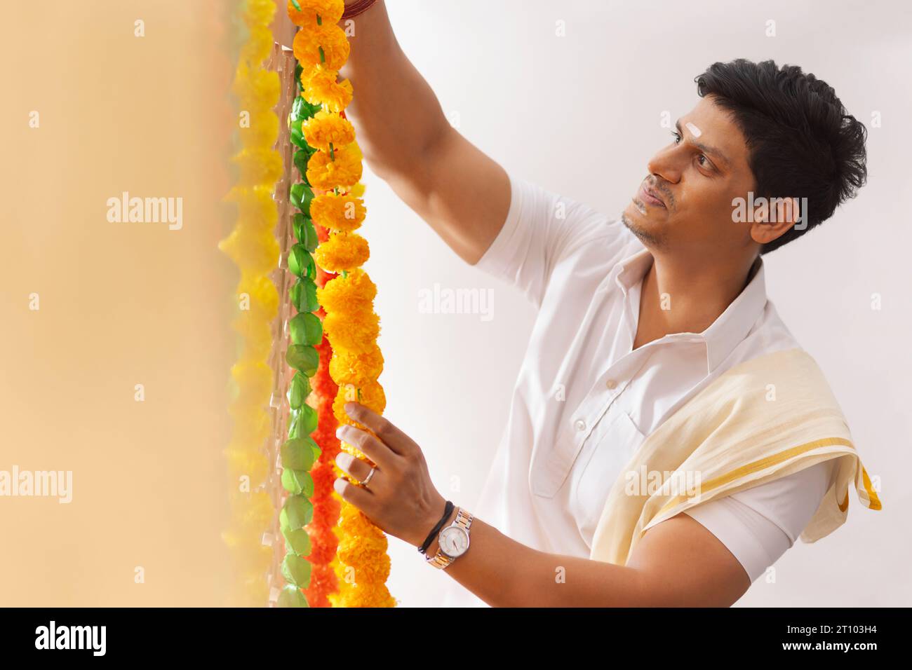 South Indian man decorating house with flower garland to celebrate Onam ...